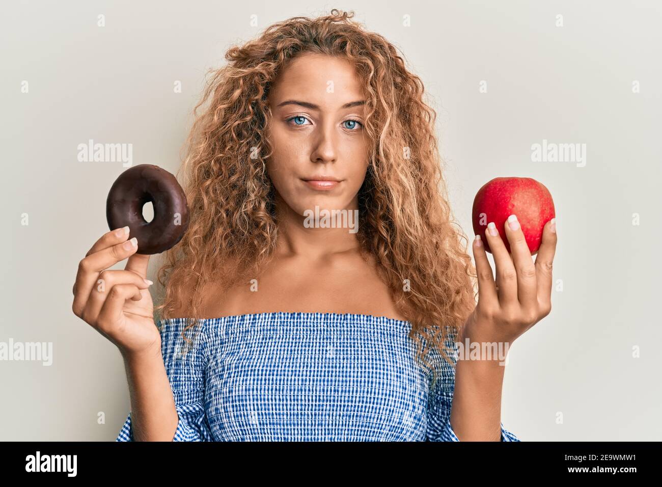 Beautiful caucasian teenager girl holding red apple and donut depressed ...