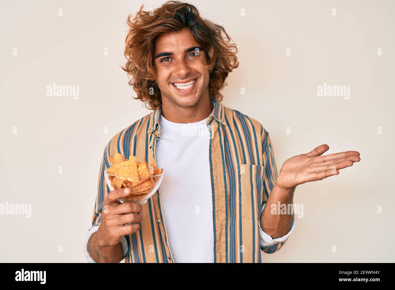 Young hispanic man holding nachos potato chips celebrating achievement ...