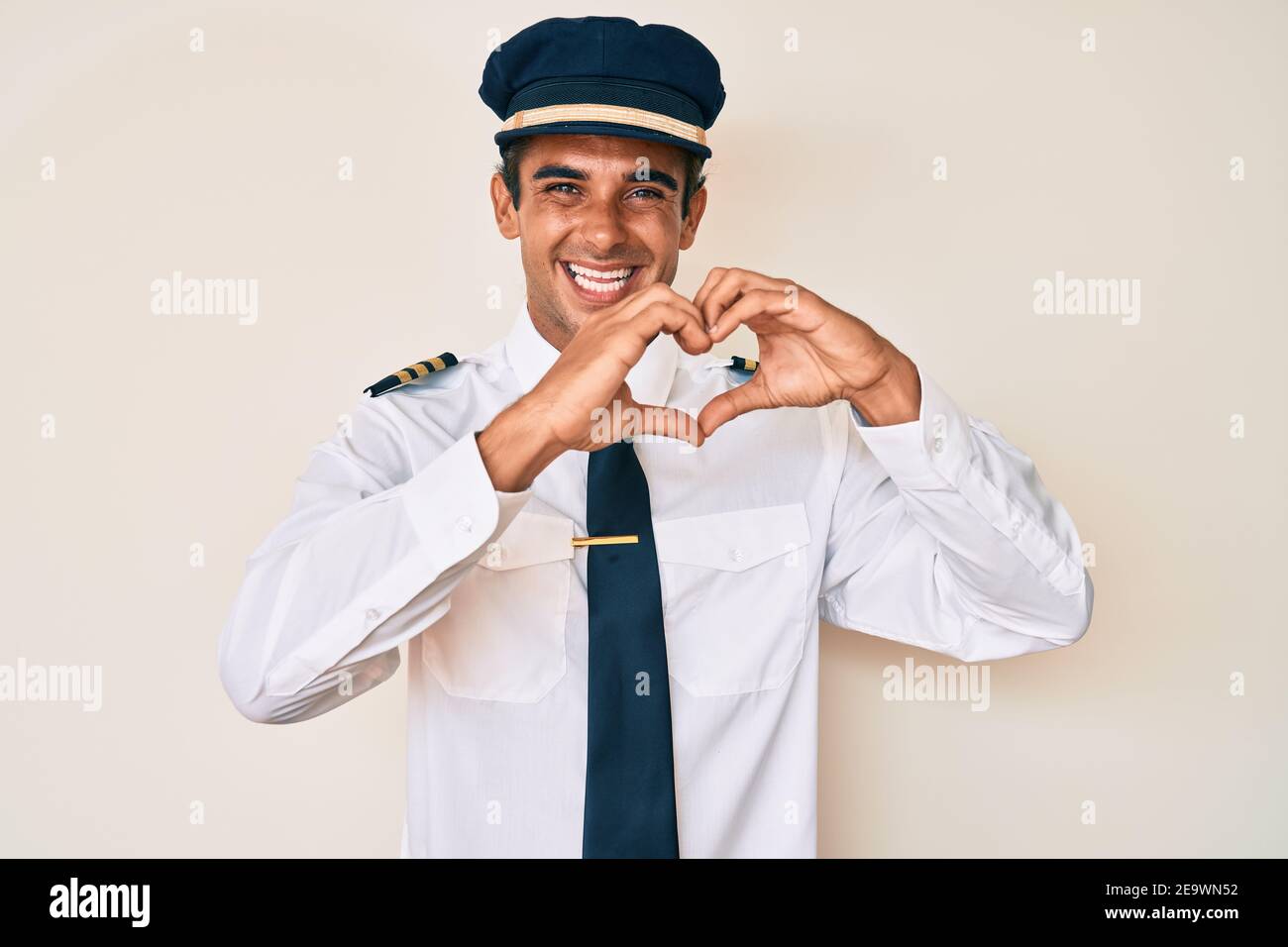 Young hispanic man wearing airplane pilot uniform smiling in love doing ...