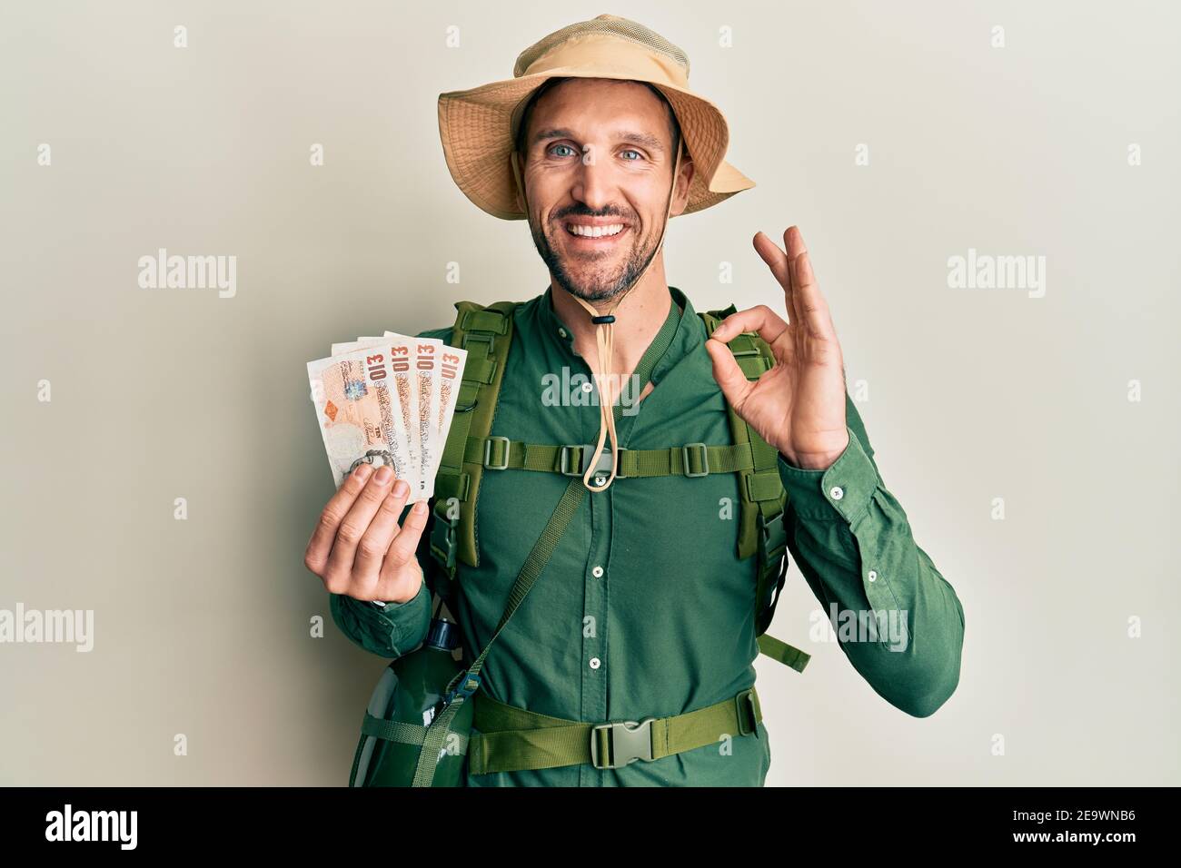 Handsome man with beard wearing explorer hat holding 10 pounds doing ok ...