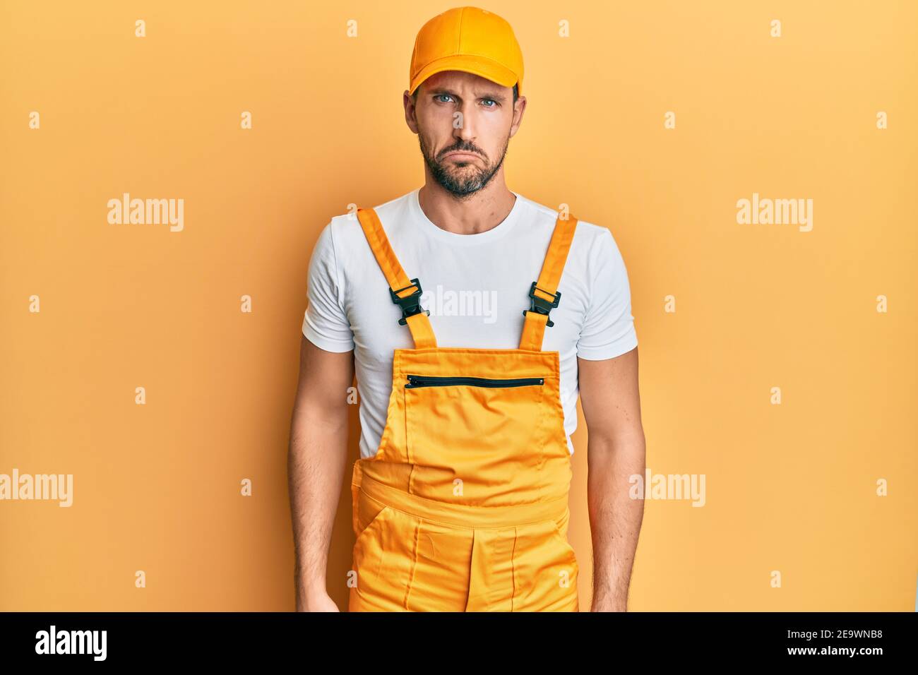 Young handsome man wearing handyman uniform over yellow background ...