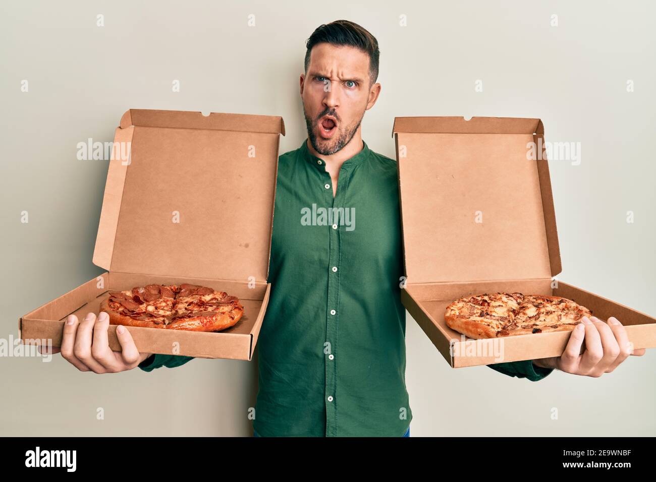 Handsome man with beard holding two italian pizzas in shock face ...