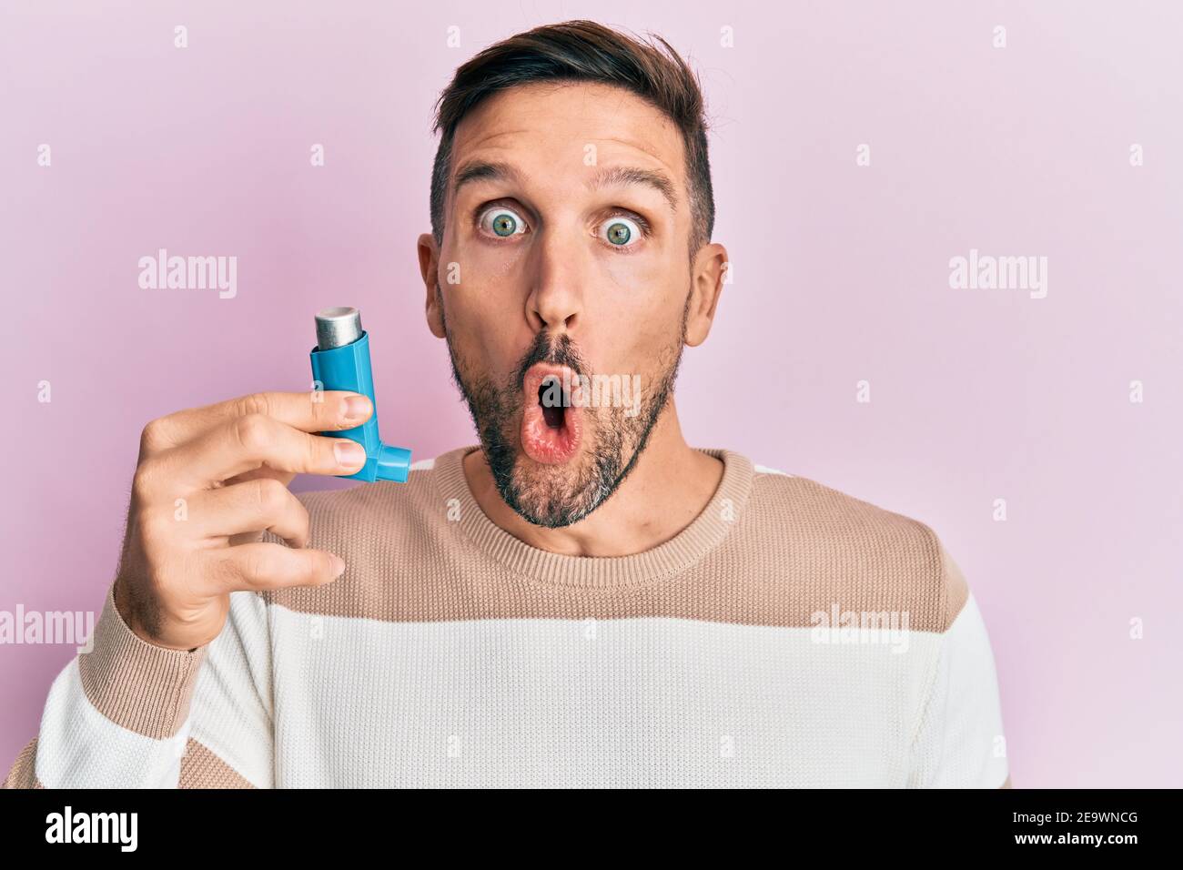 Handsome man with beard holding medical asthma inhaler scared and ...