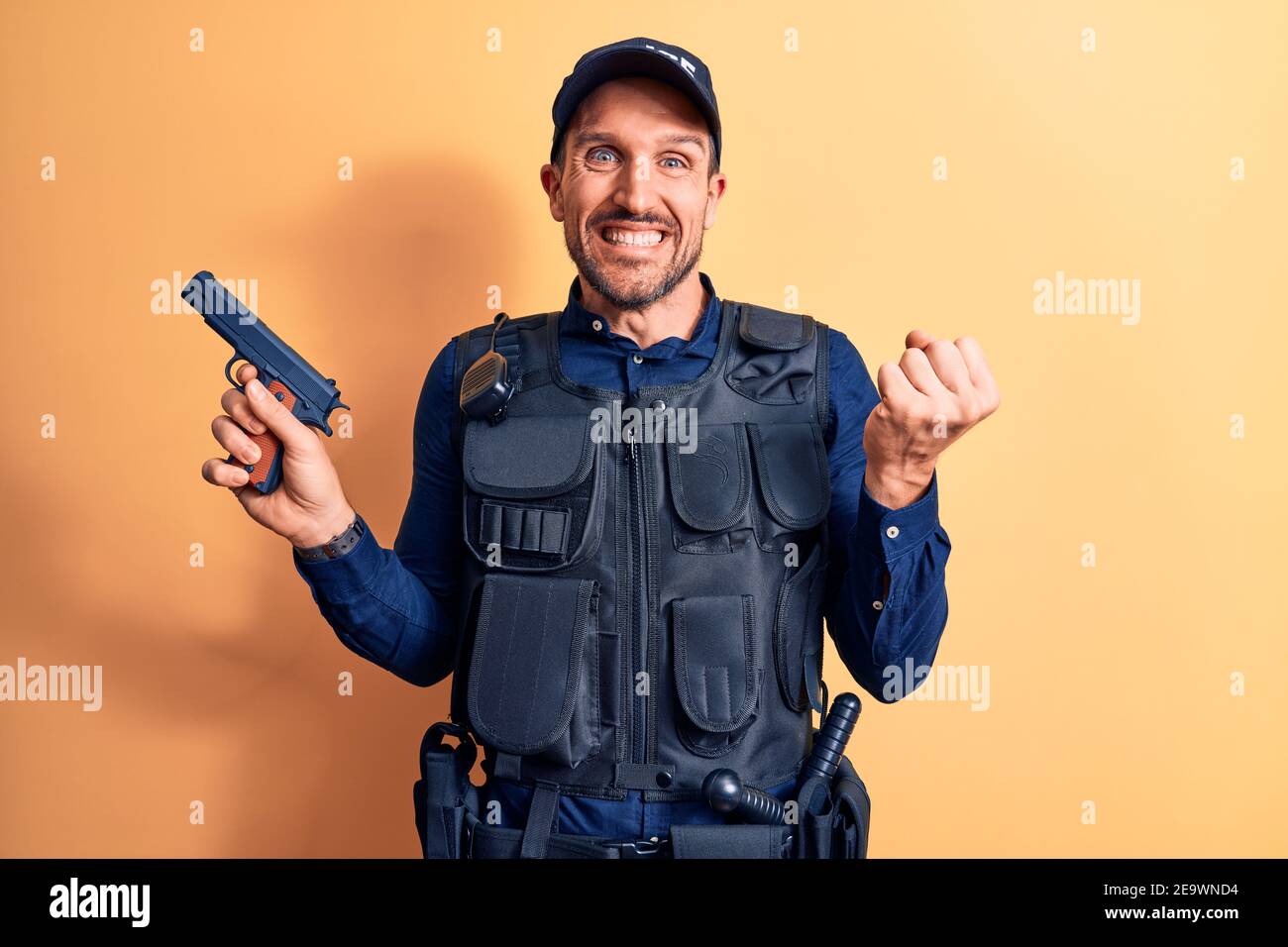 Handsome policeman wearing uniform and bulletprof holding gun over ...
