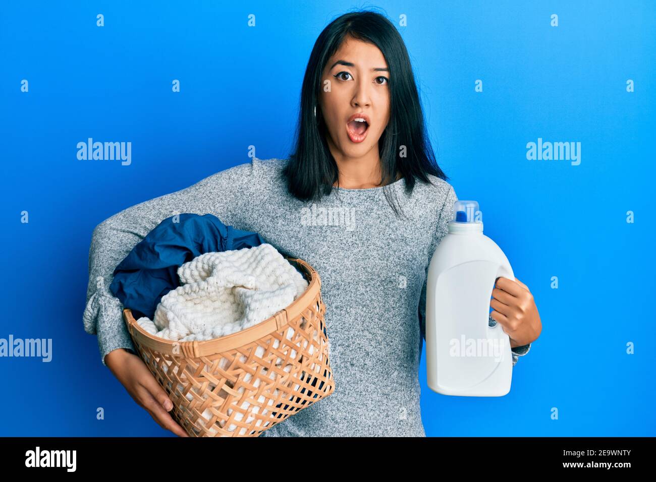 Beautiful asian young woman holding laundry basket and detergent bottle ...