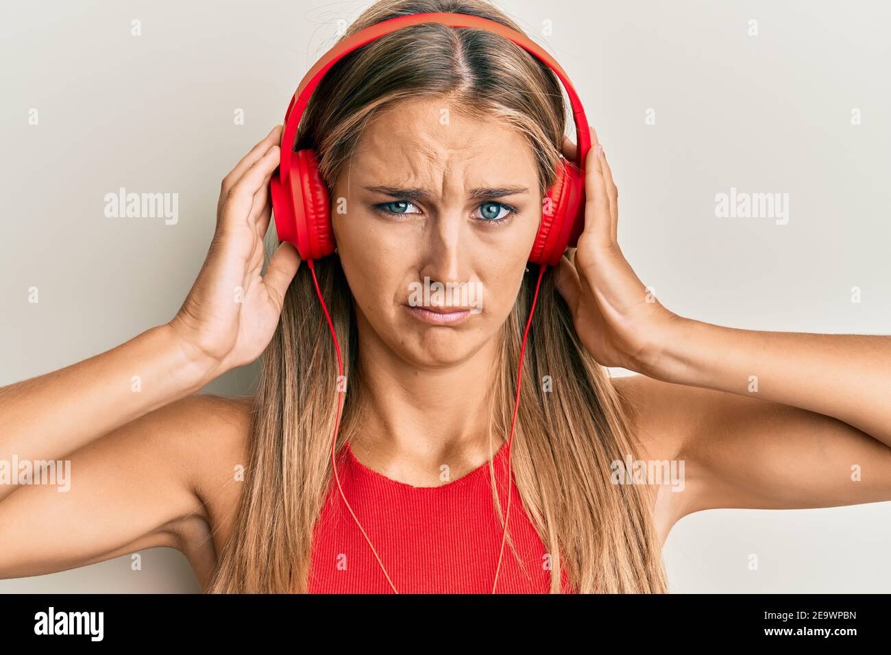 Young blonde woman listening to music using headphones depressed and ...