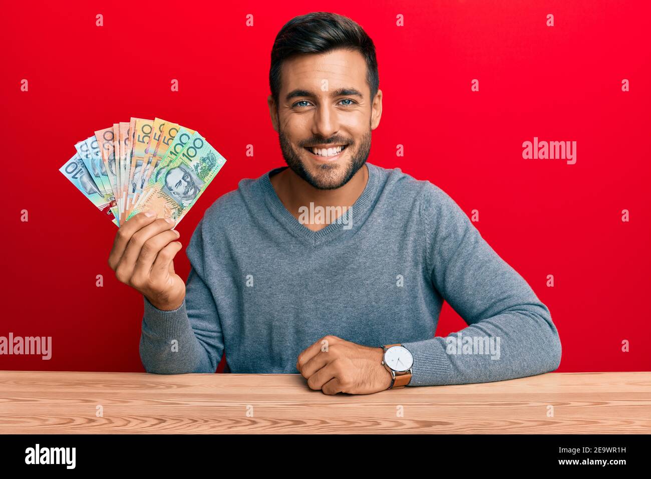 Handsome hispanic man holding australian dollars looking positive and ...