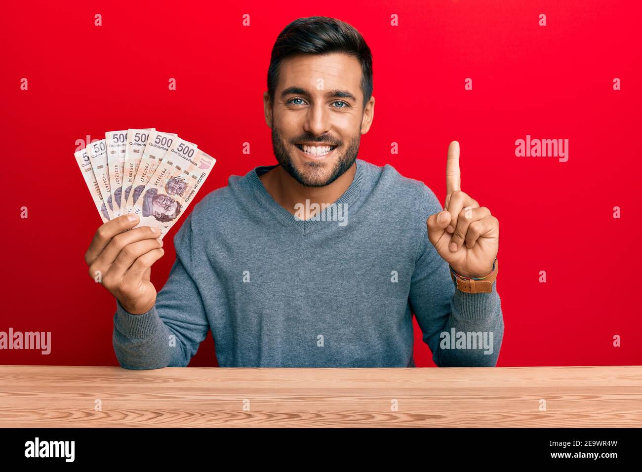 Handsome hispanic man holding mexican pesos smiling with an idea or ...