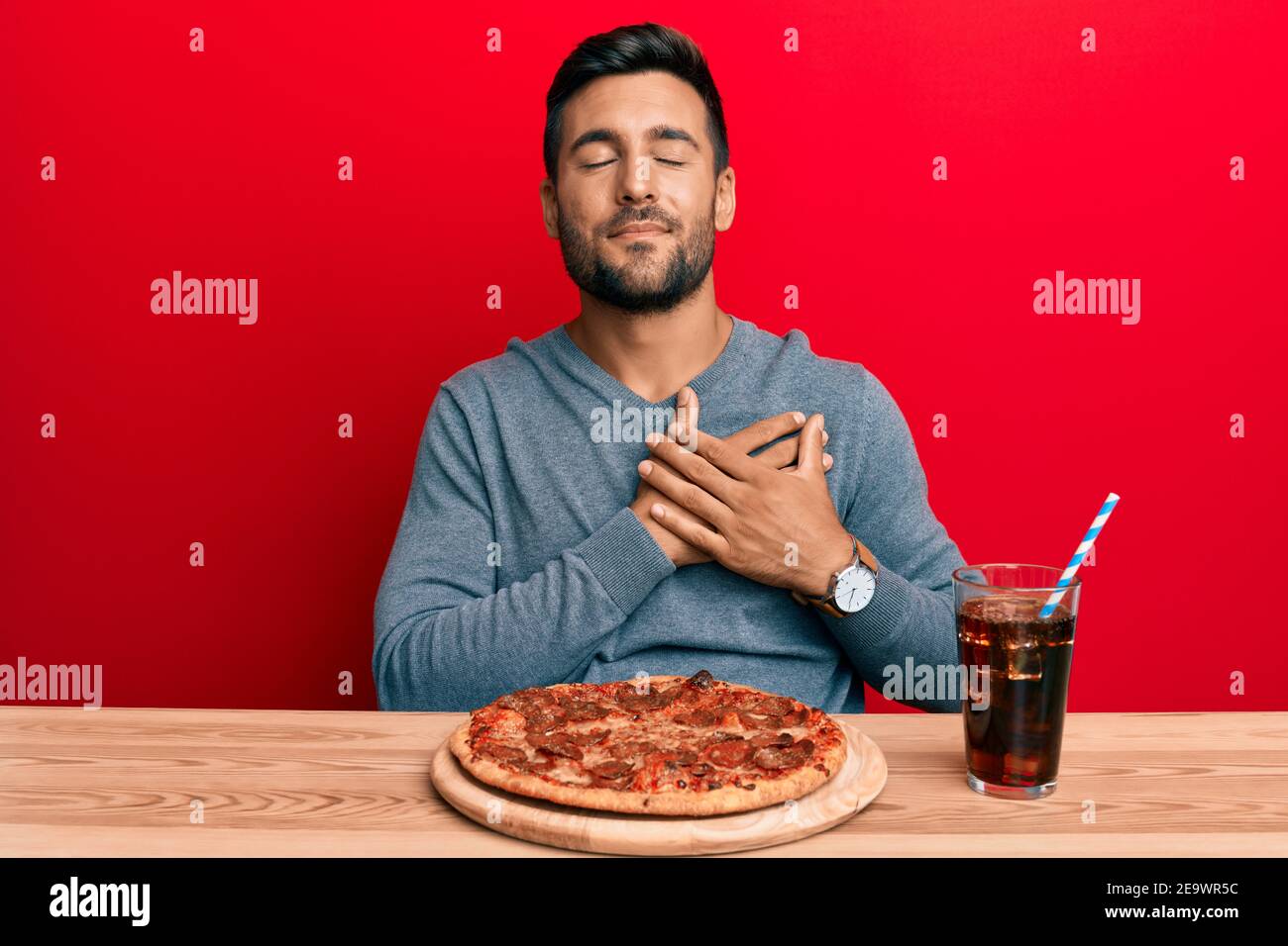 Handsome hispanic man eating tasty pepperoni pizza smiling with hands ...