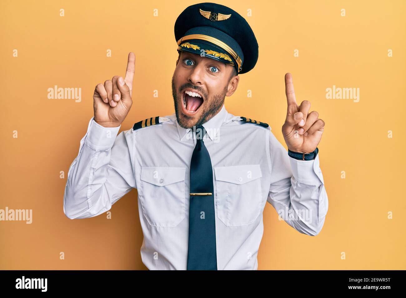 Handsome hispanic man wearing airplane pilot uniform smiling amazed and ...