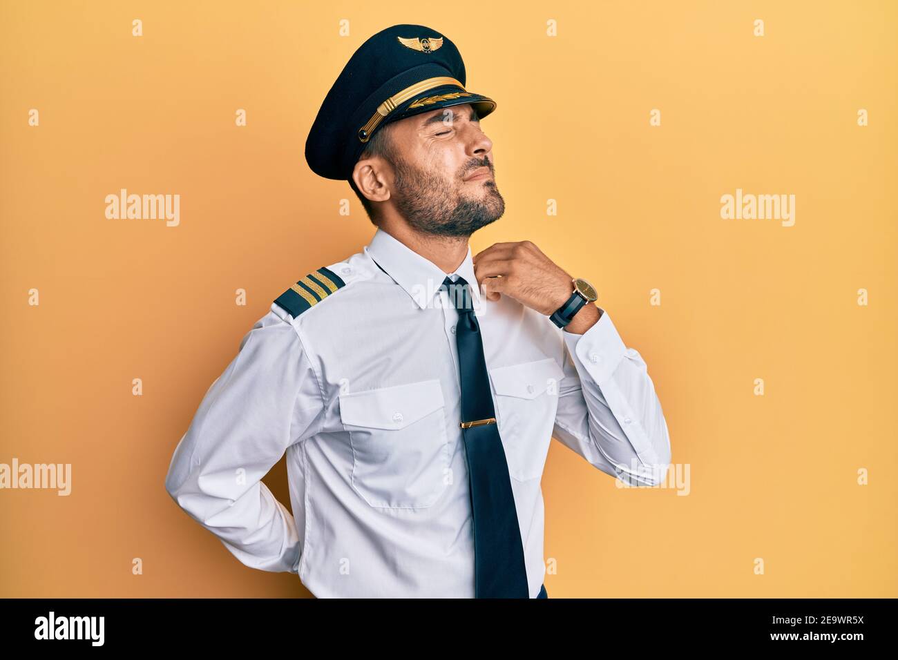 Handsome hispanic man wearing airplane pilot uniform suffering of neck ...