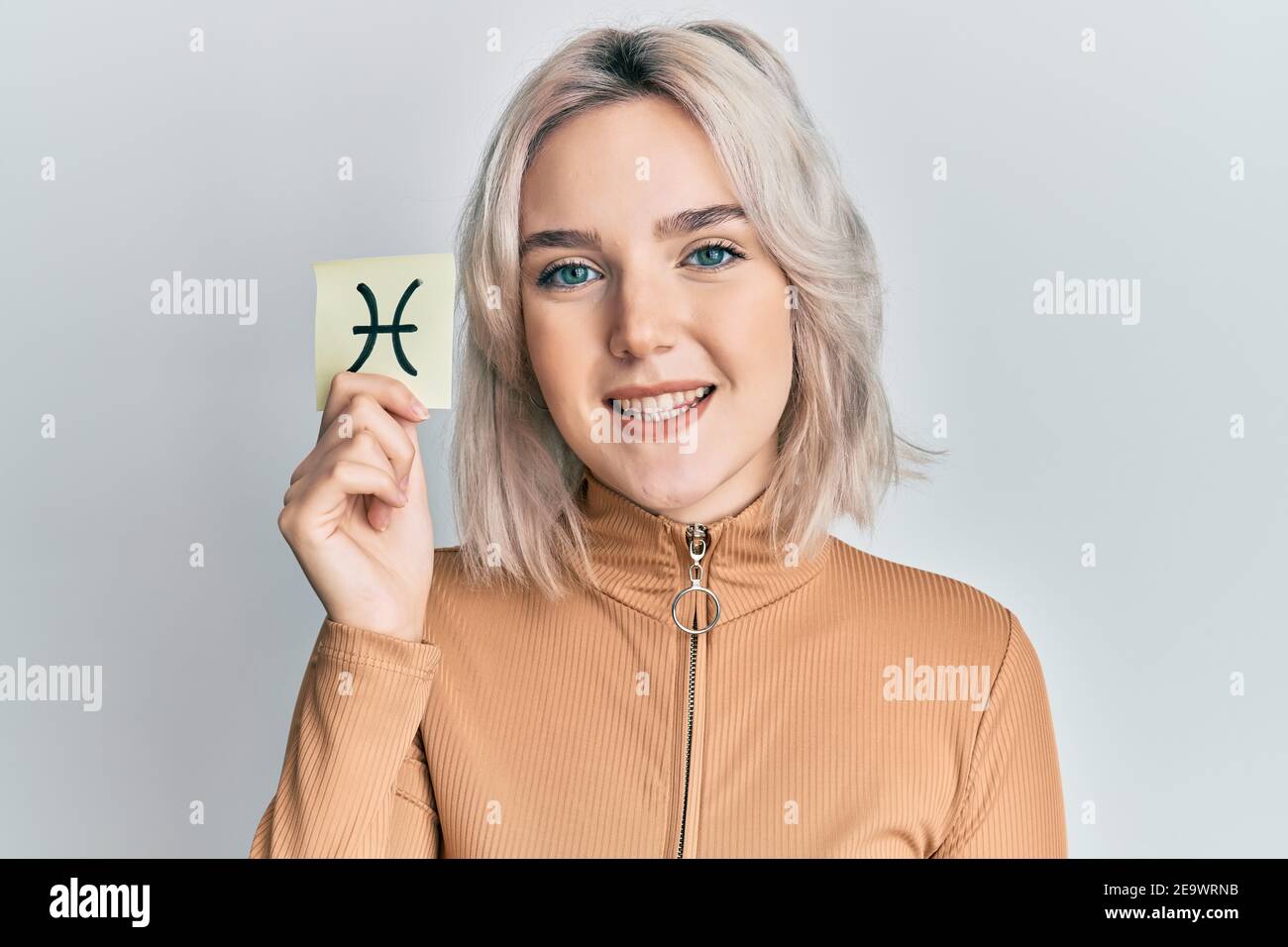 Young blonde girl holding paper with pisces zodiac sign looking ...