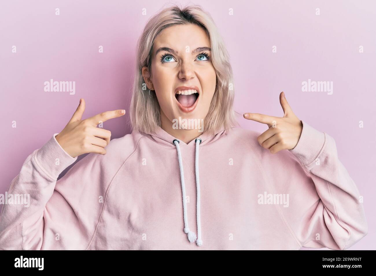 Young blonde girl pointing mouth with fingers angry and mad screaming ...