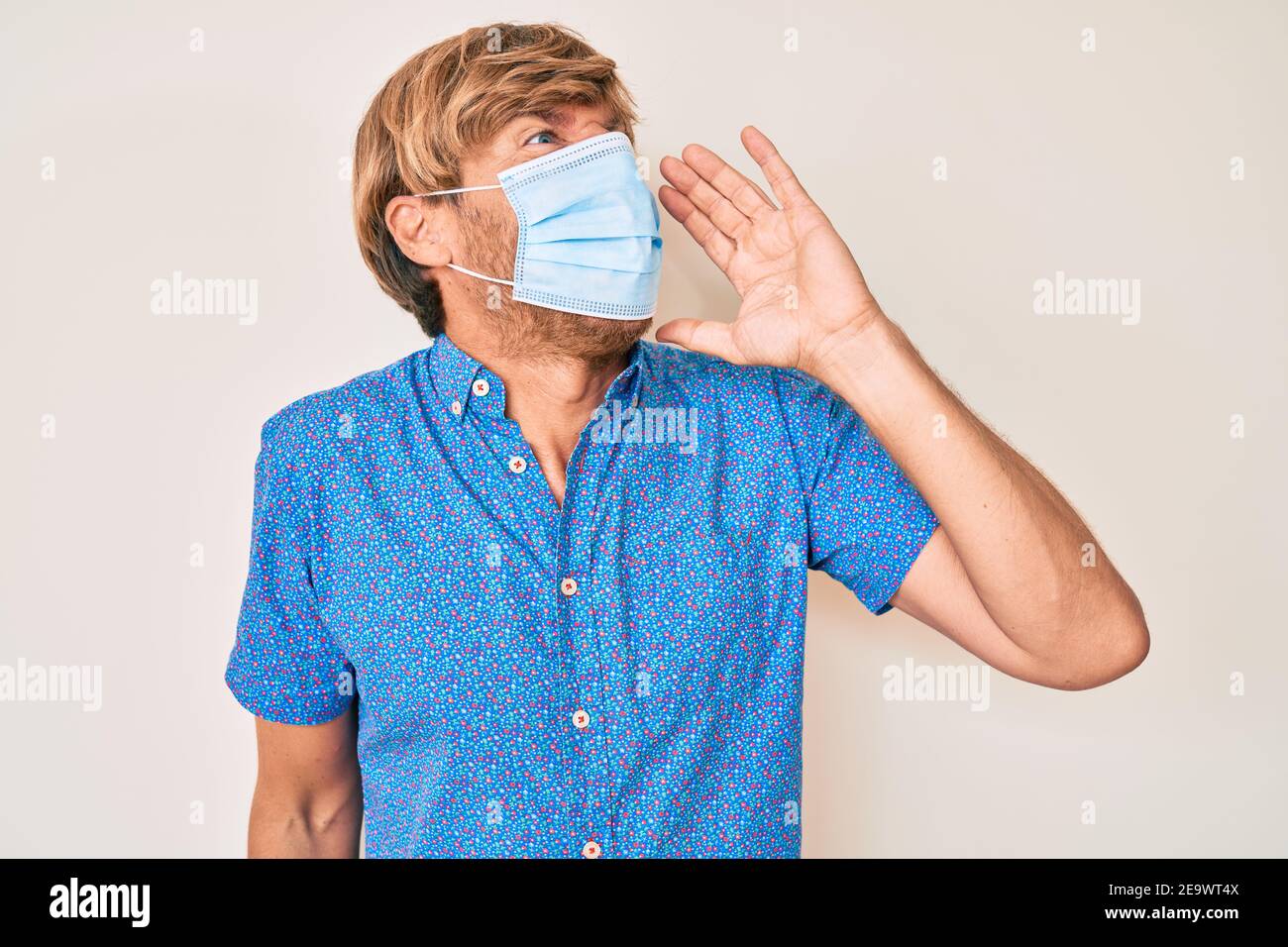Young blond man wearing medical mask shouting and screaming loud to ...