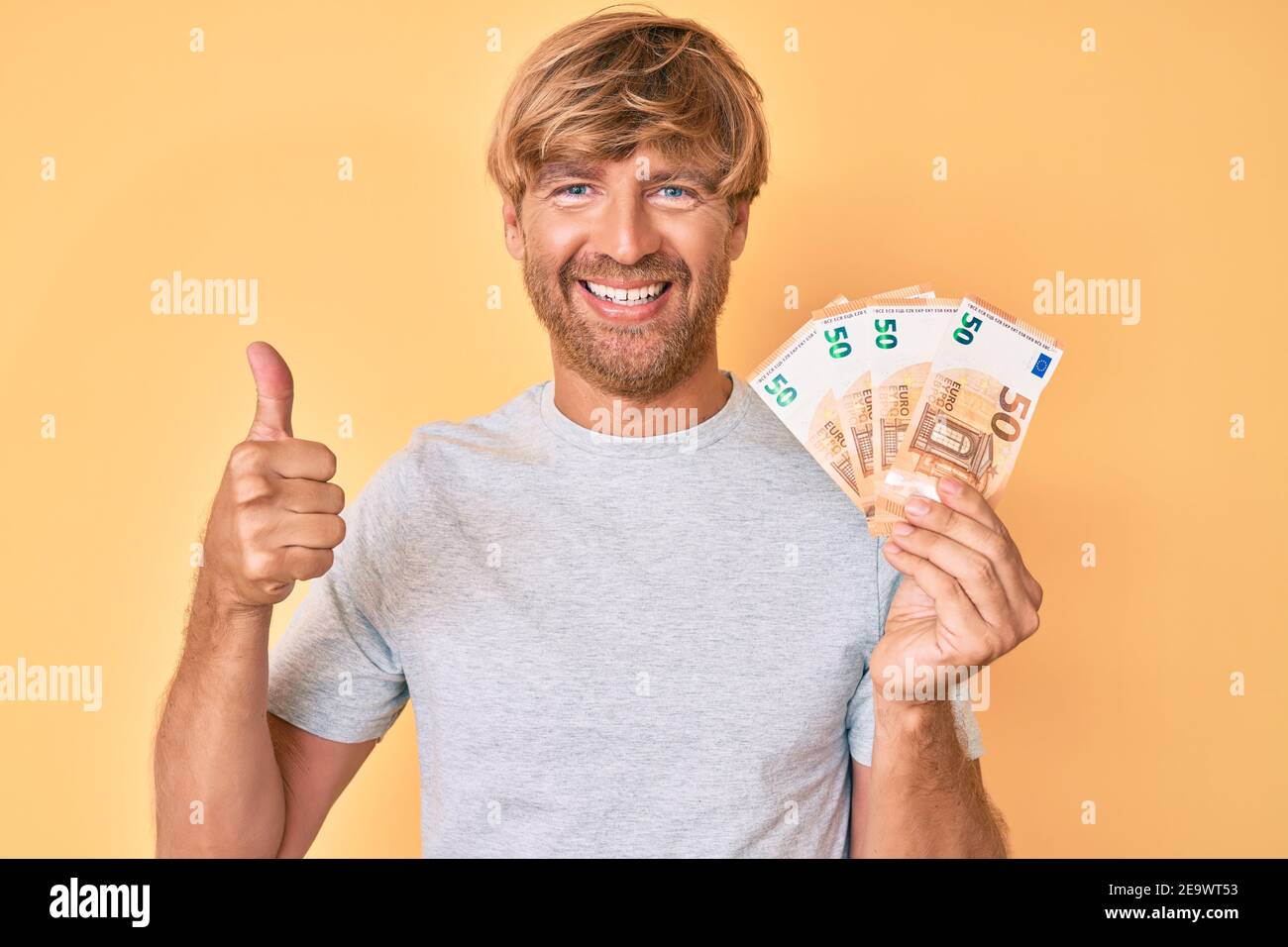 Young blond man holding euro banknotes smiling happy and positive ...