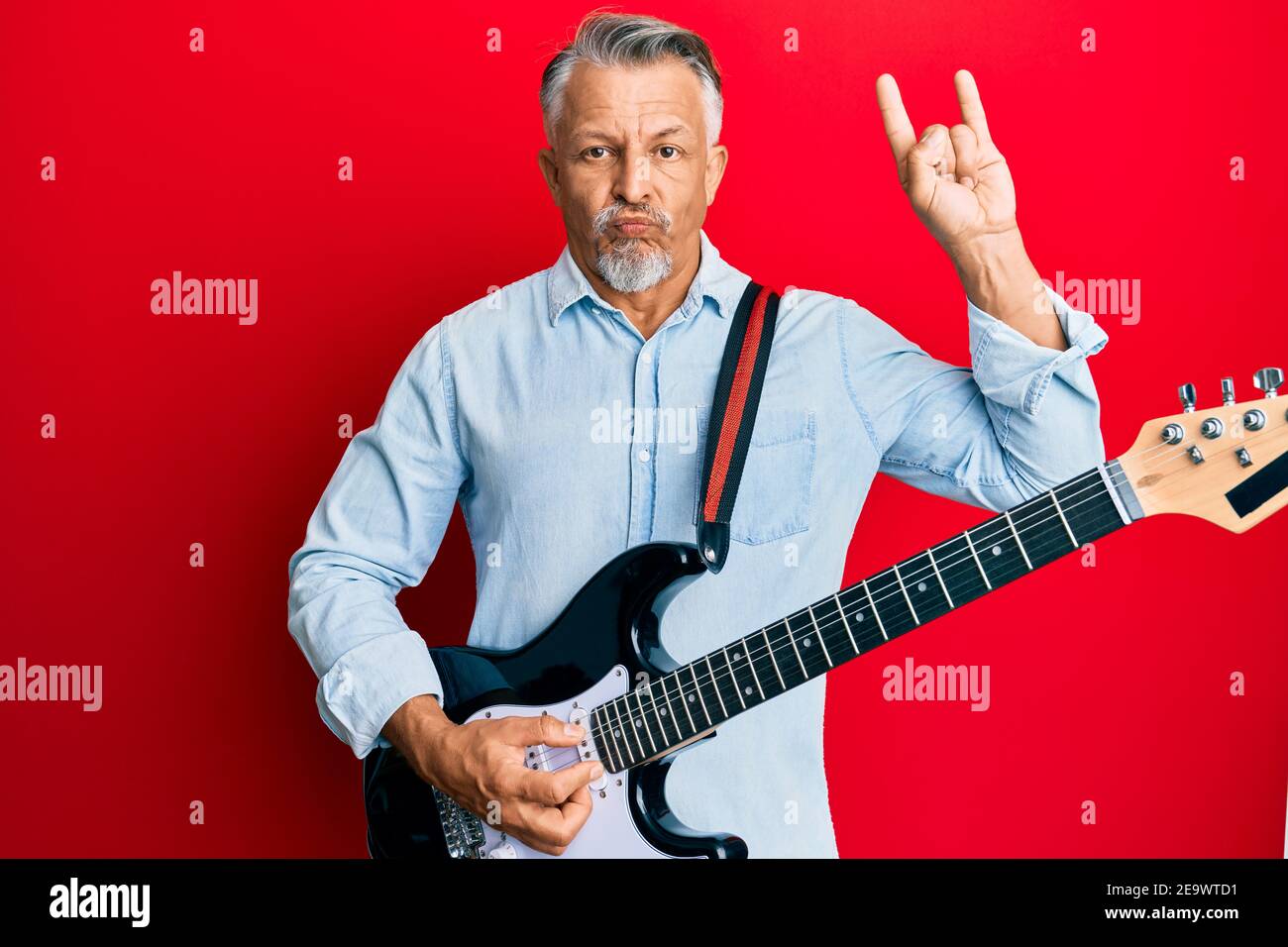 Middle age grey-haired man playing electric guitar doing rock sign ...