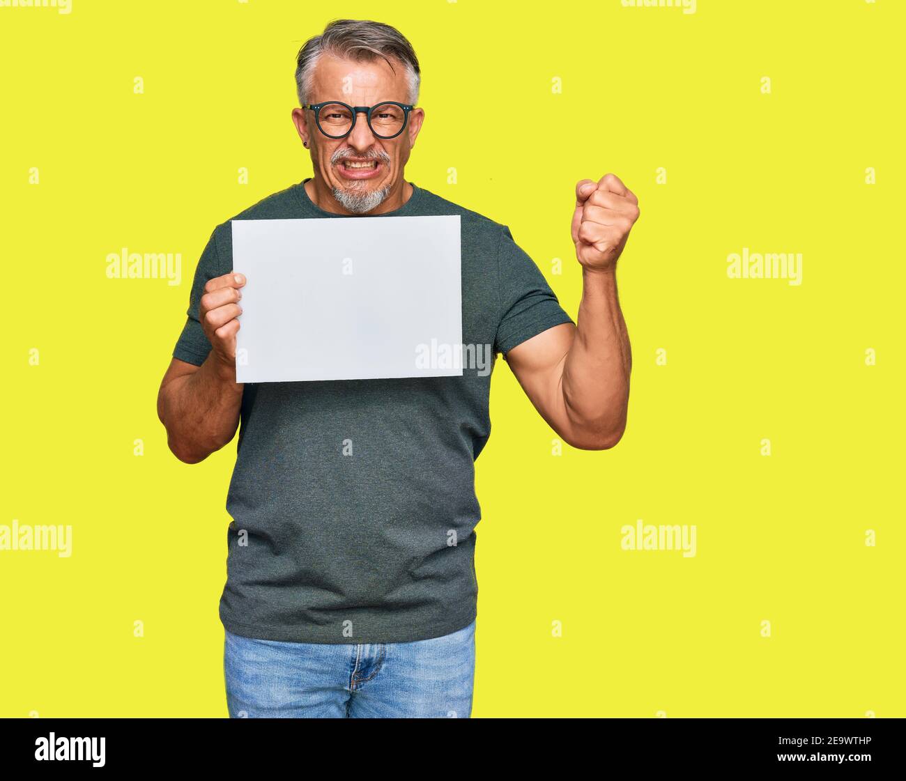 Middle age grey-haired man holding blank empty banner annoyed and ...