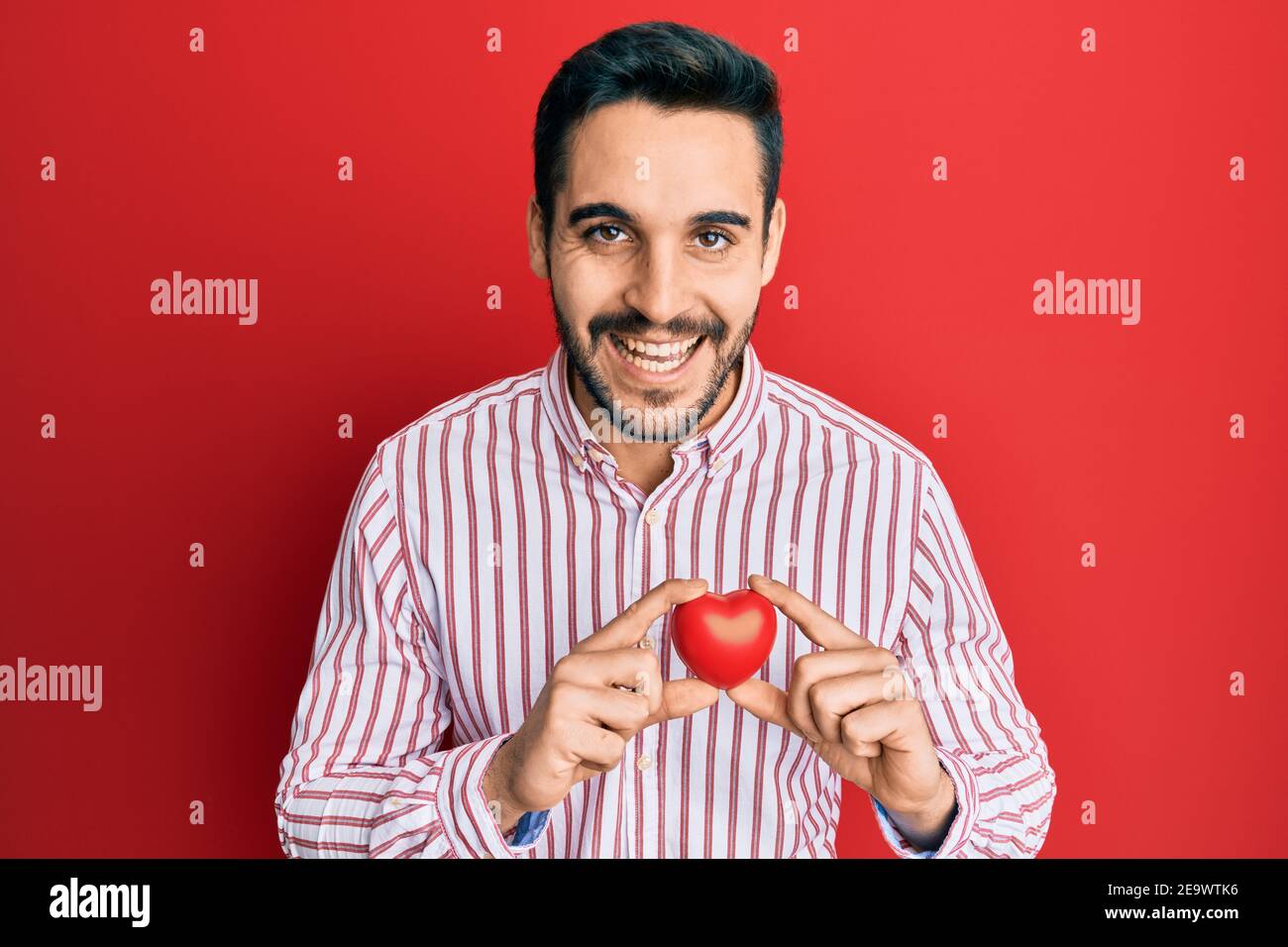 Young hispanic man holding heart smiling and laughing hard out loud ...