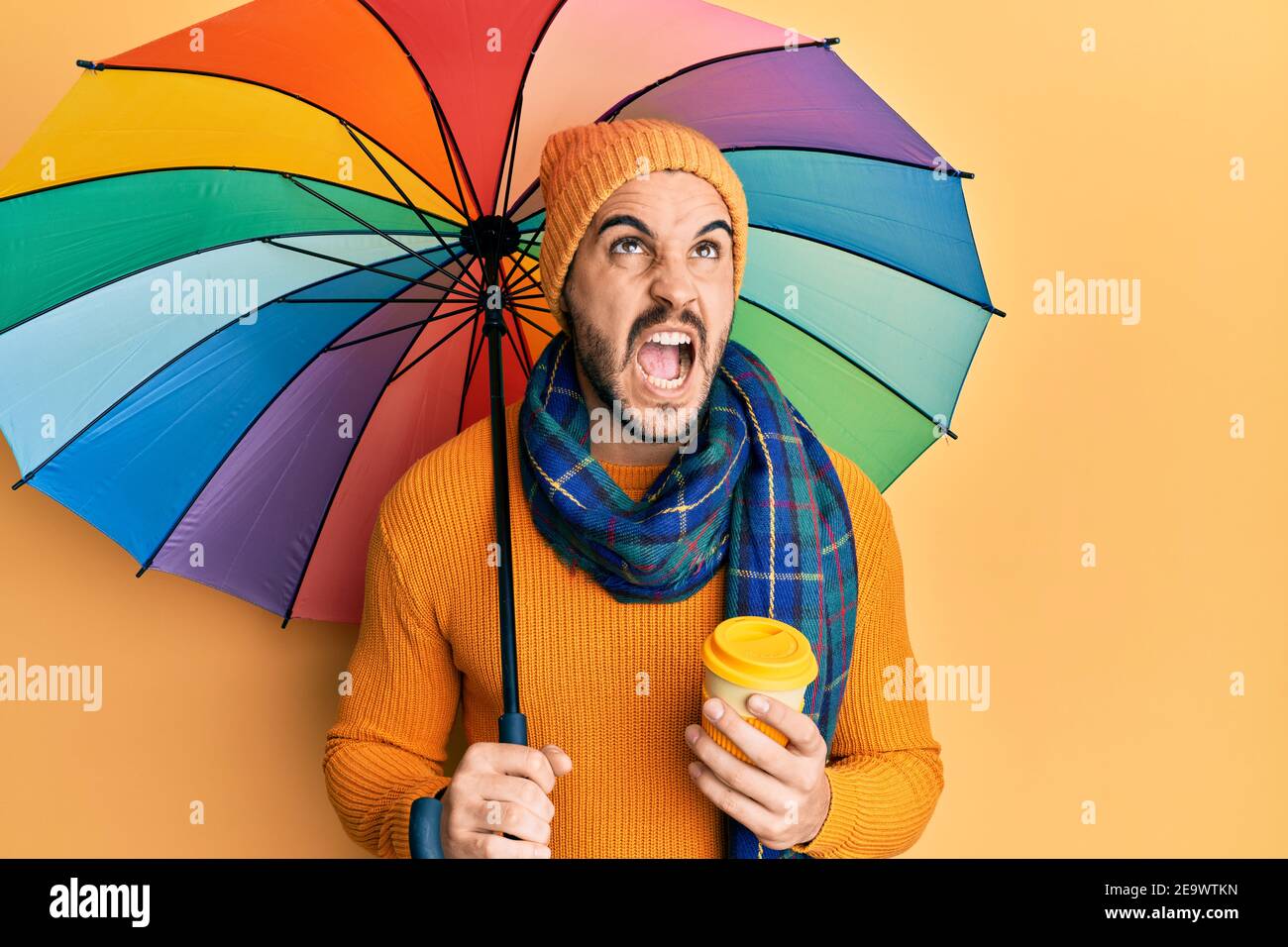 Young hispanic man holding colorful umbrella drinking take away coffee ...