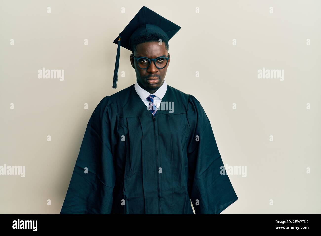 Handsome black man wearing graduation cap and ceremony robe depressed ...