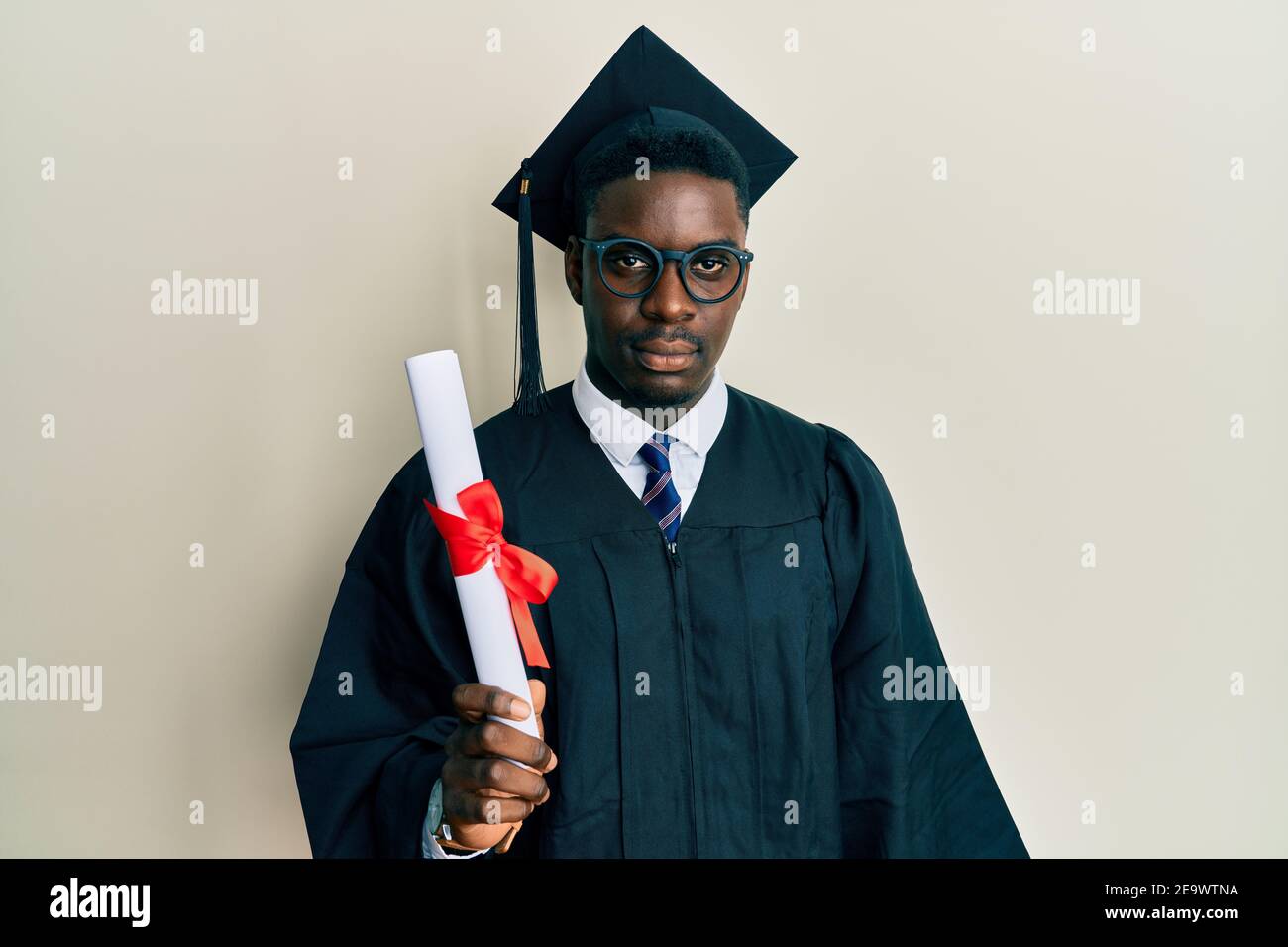 Handsome black man wearing graduation cap and ceremony robe holding ...