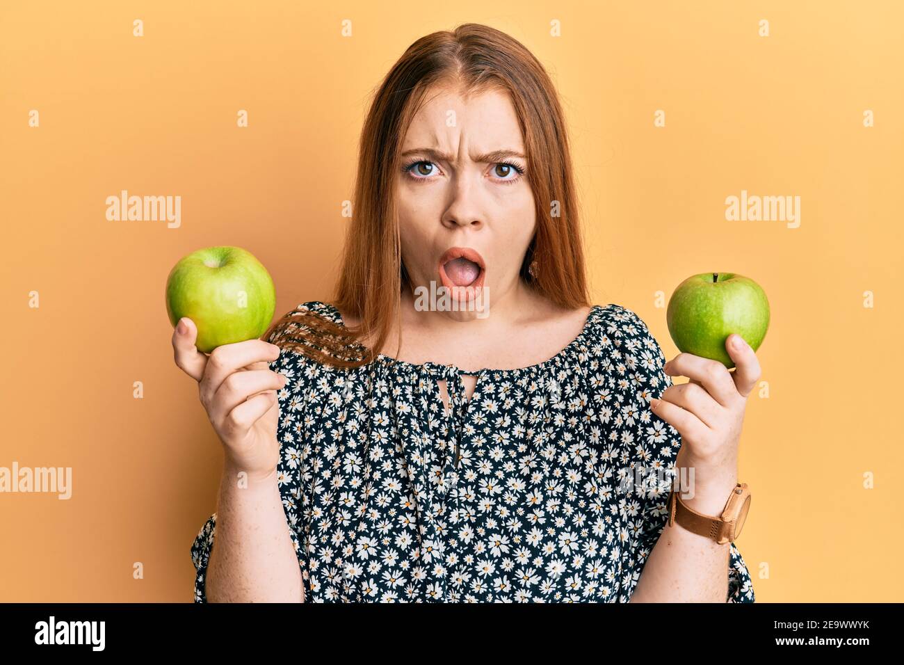 Young beautiful redhead woman holding green apples in shock face ...