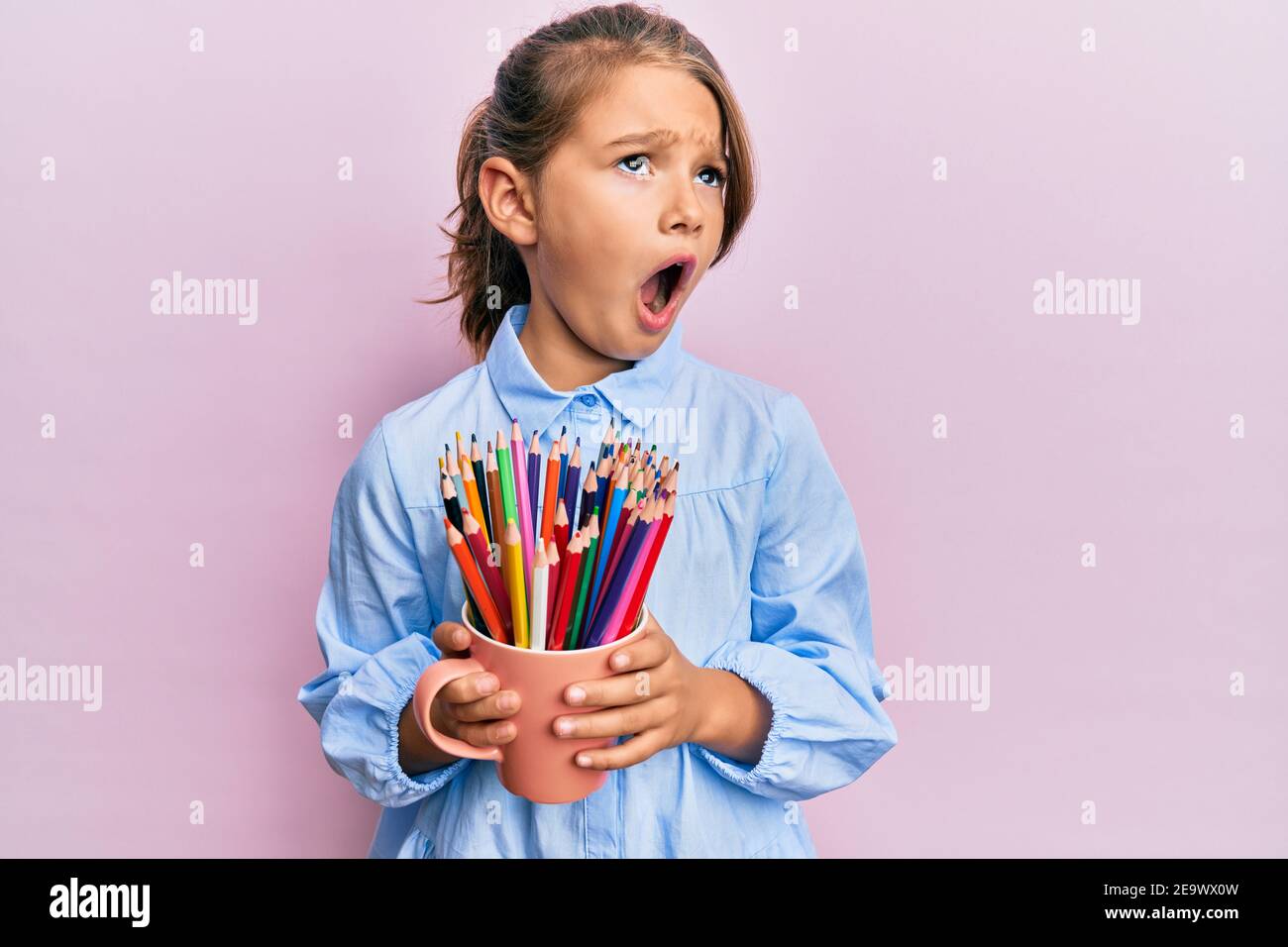 Little beautiful girl holding colored pencils angry and mad screaming ...