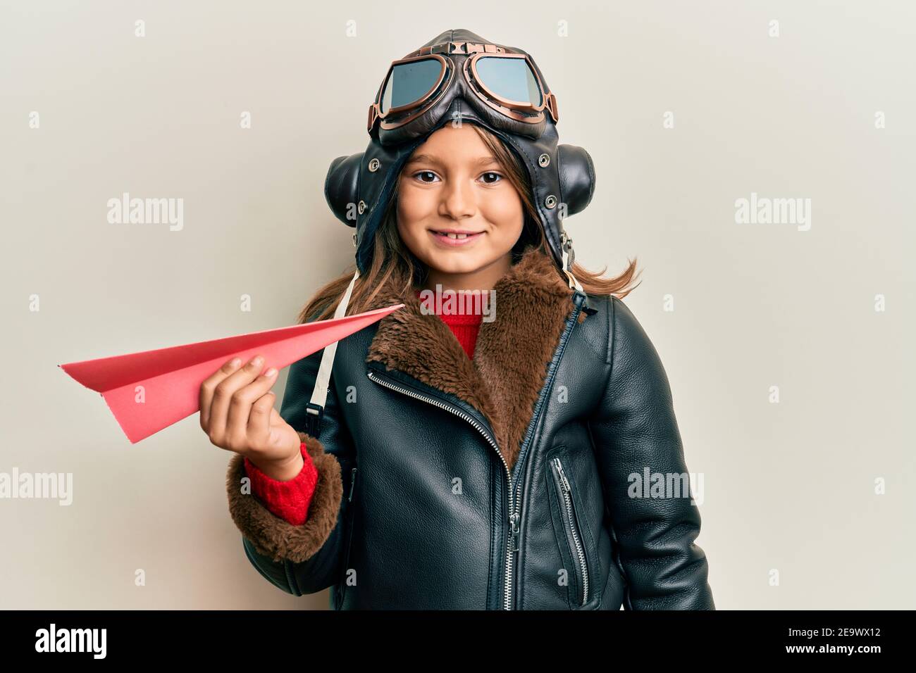 Little beautiful girl wearing pilot uniform holding paper plane looking ...