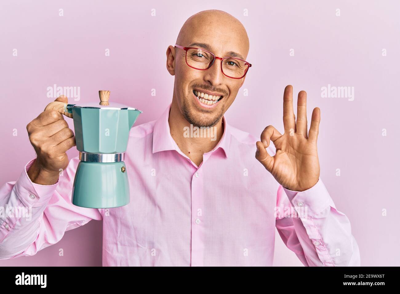 Bald man with beard drinking italian coffee doing ok sign with fingers ...