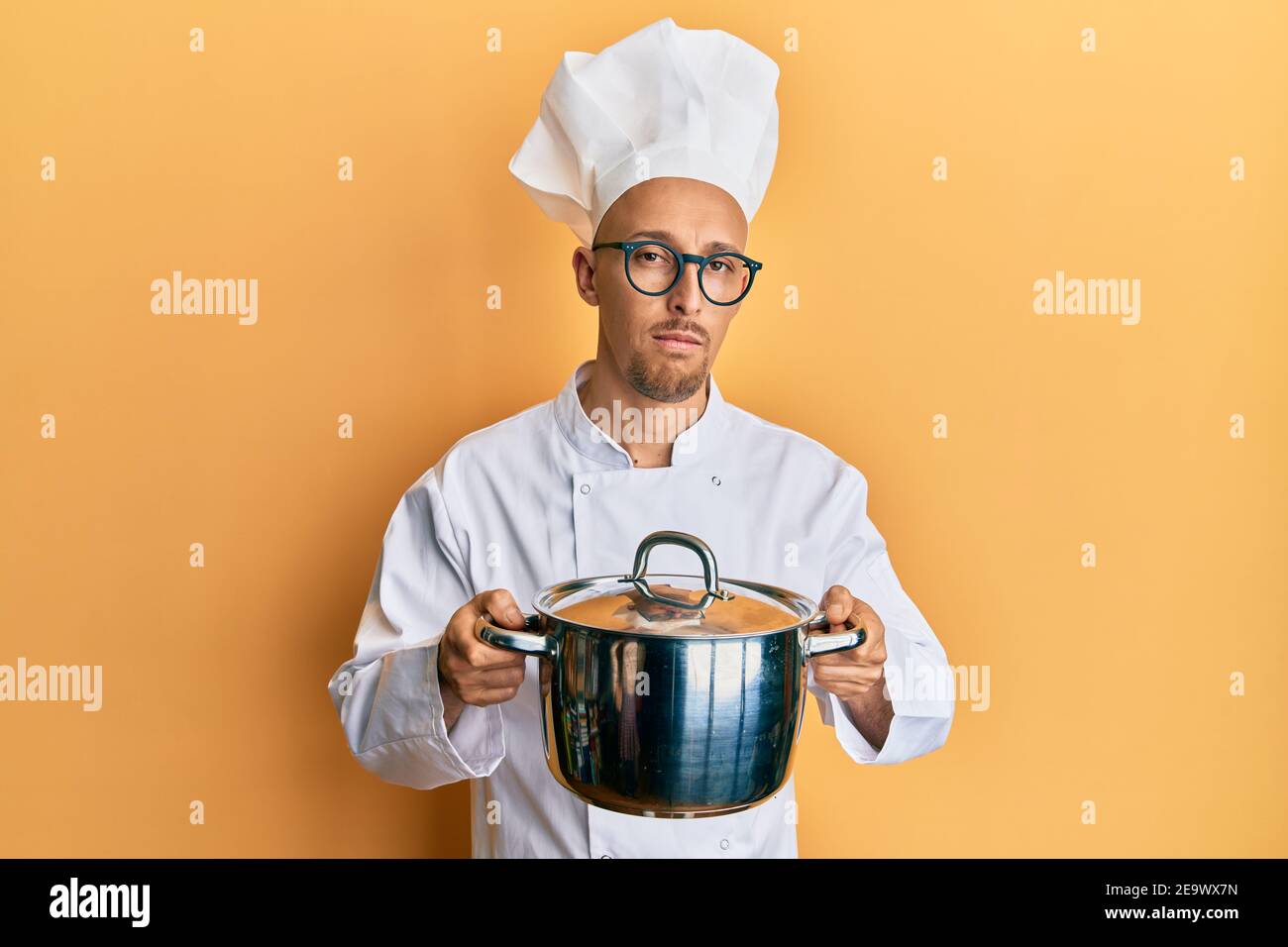 Bald man with beard wearing professional cook holding cooking pot ...