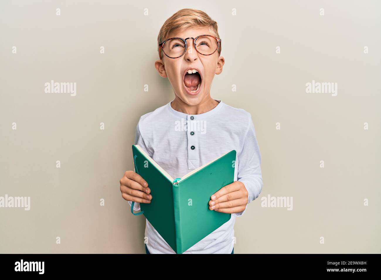 Little caucasian boy kid reading a book wearing glasses angry and mad ...