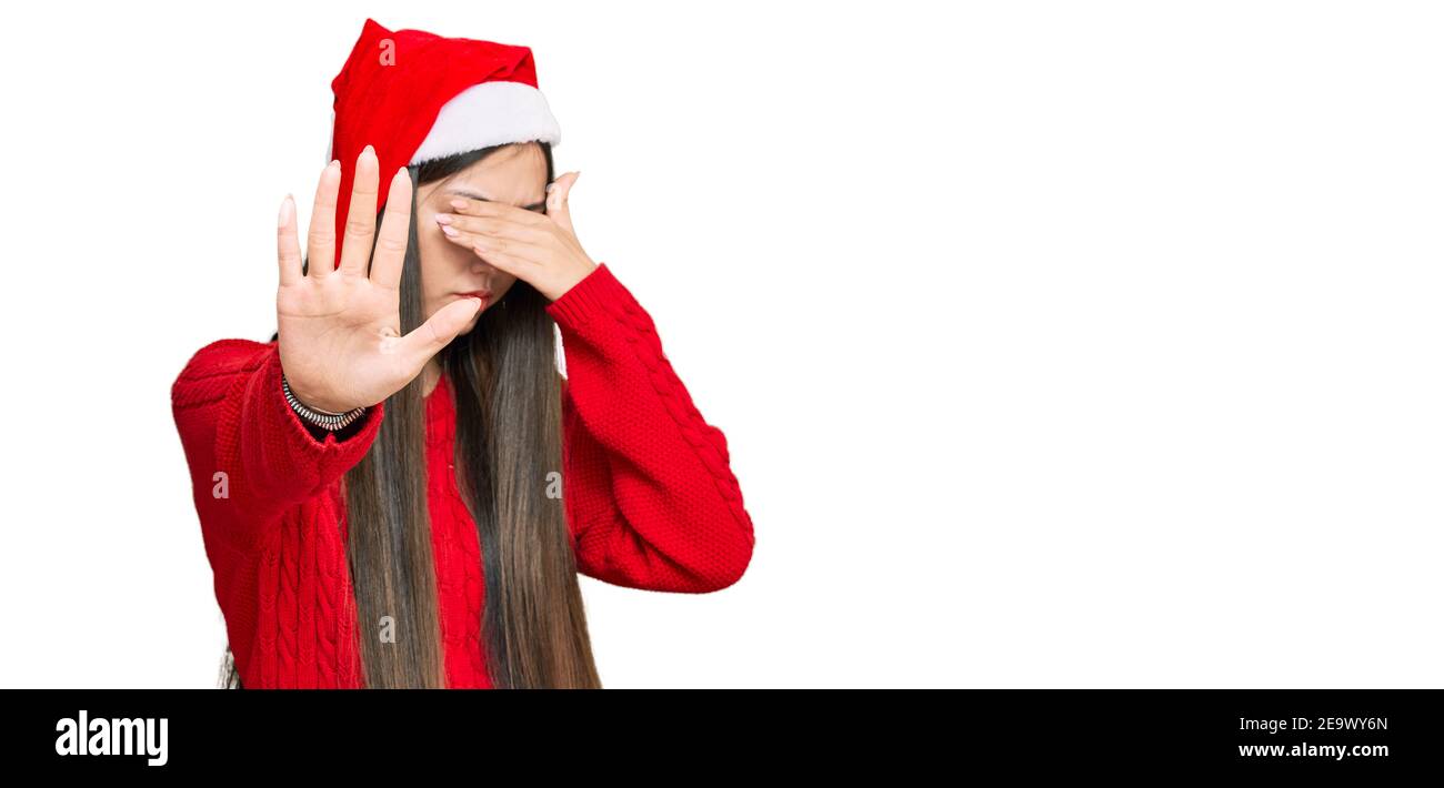 Young chinese woman wearing christmas hat covering eyes with hands and ...