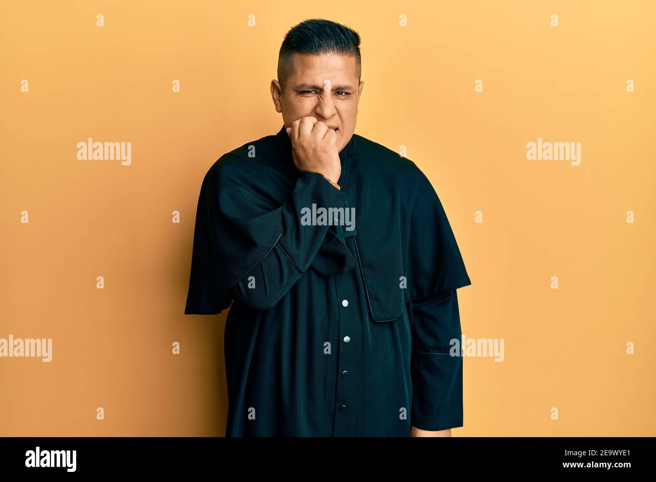 Young latin priest man standing over yellow background looking stressed ...