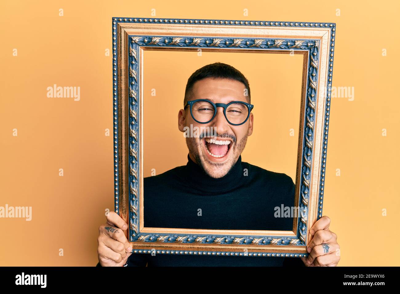 Handsome man with tattoos holding empty frame smiling and laughing hard ...
