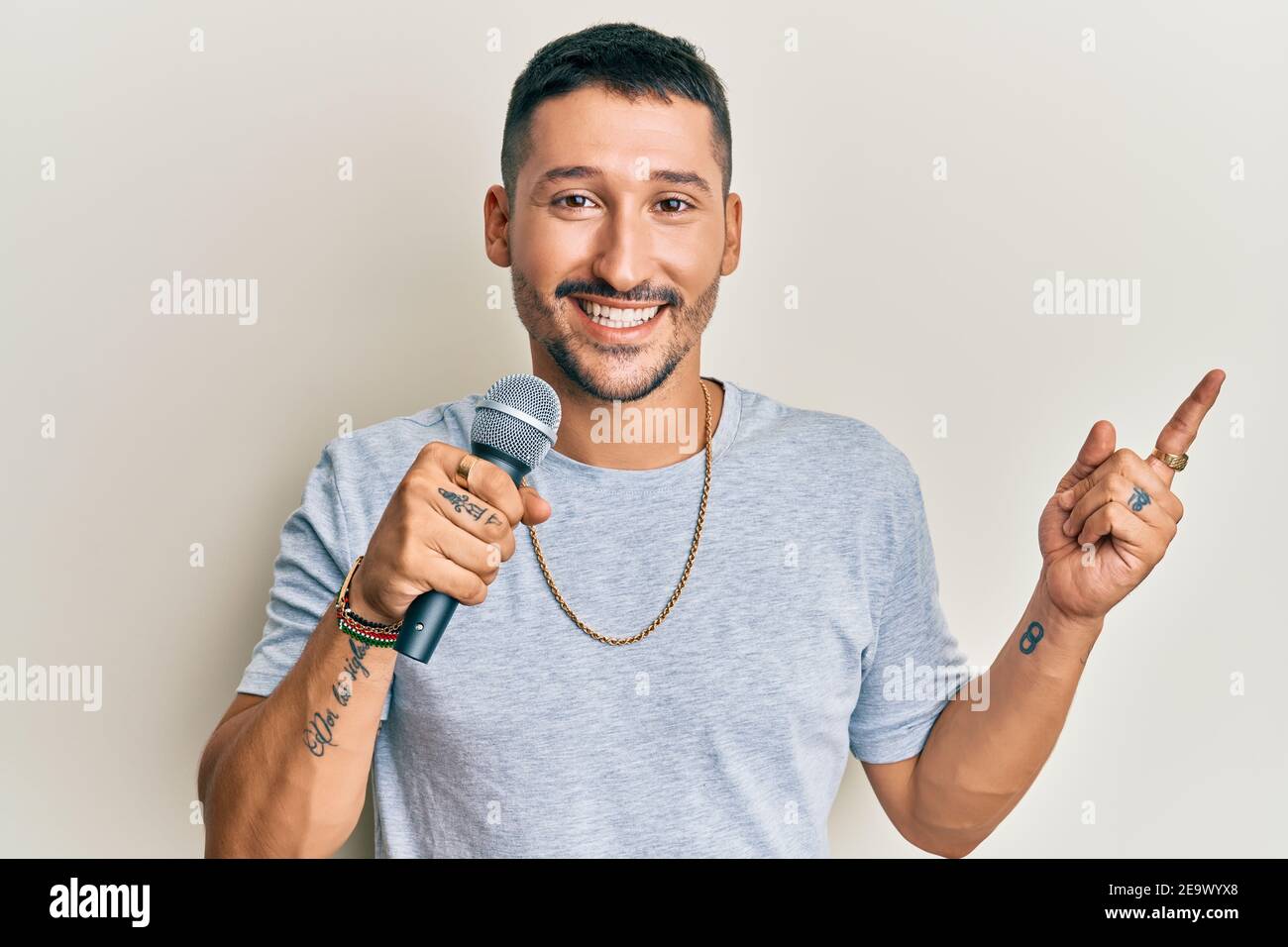 Handsome man with tattoos singing song using microphone smiling happy ...