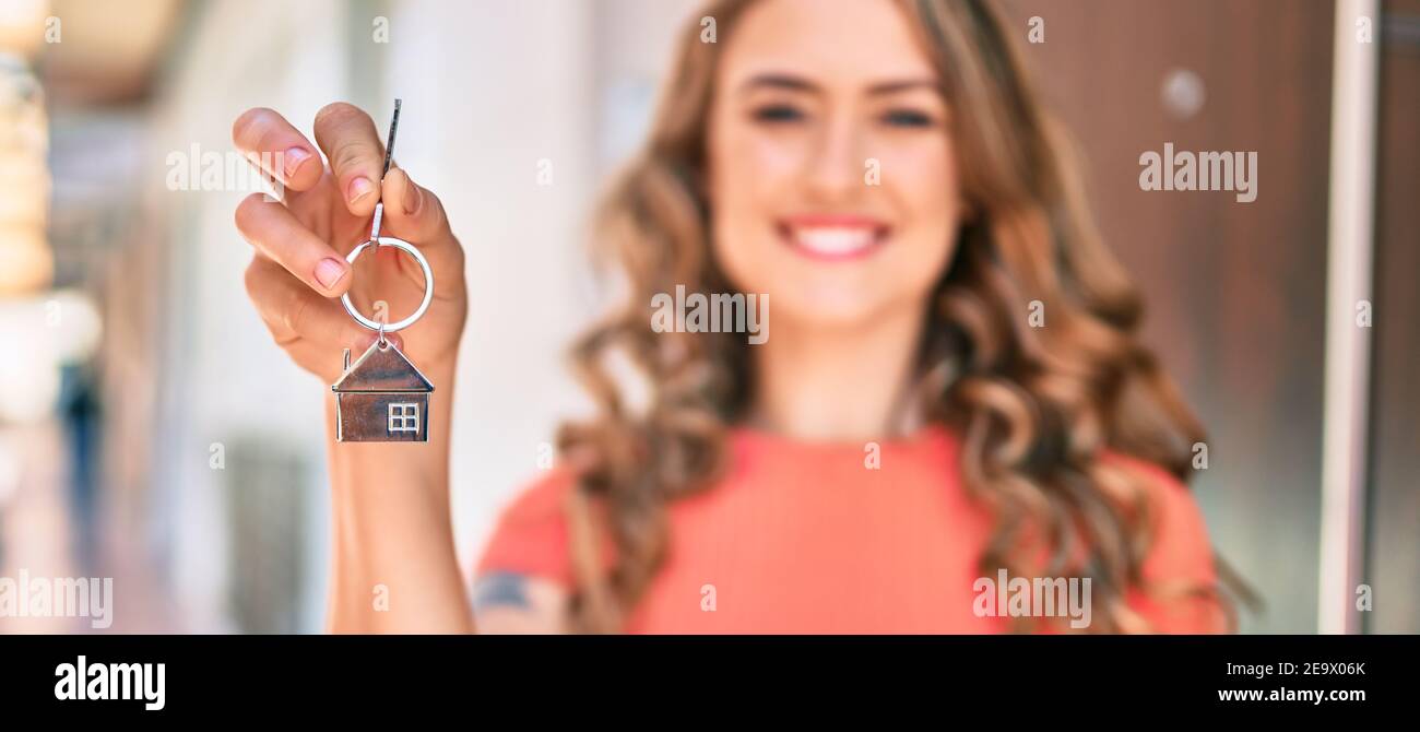 Young blonde girl smiling happy holding key of new house standing at ...