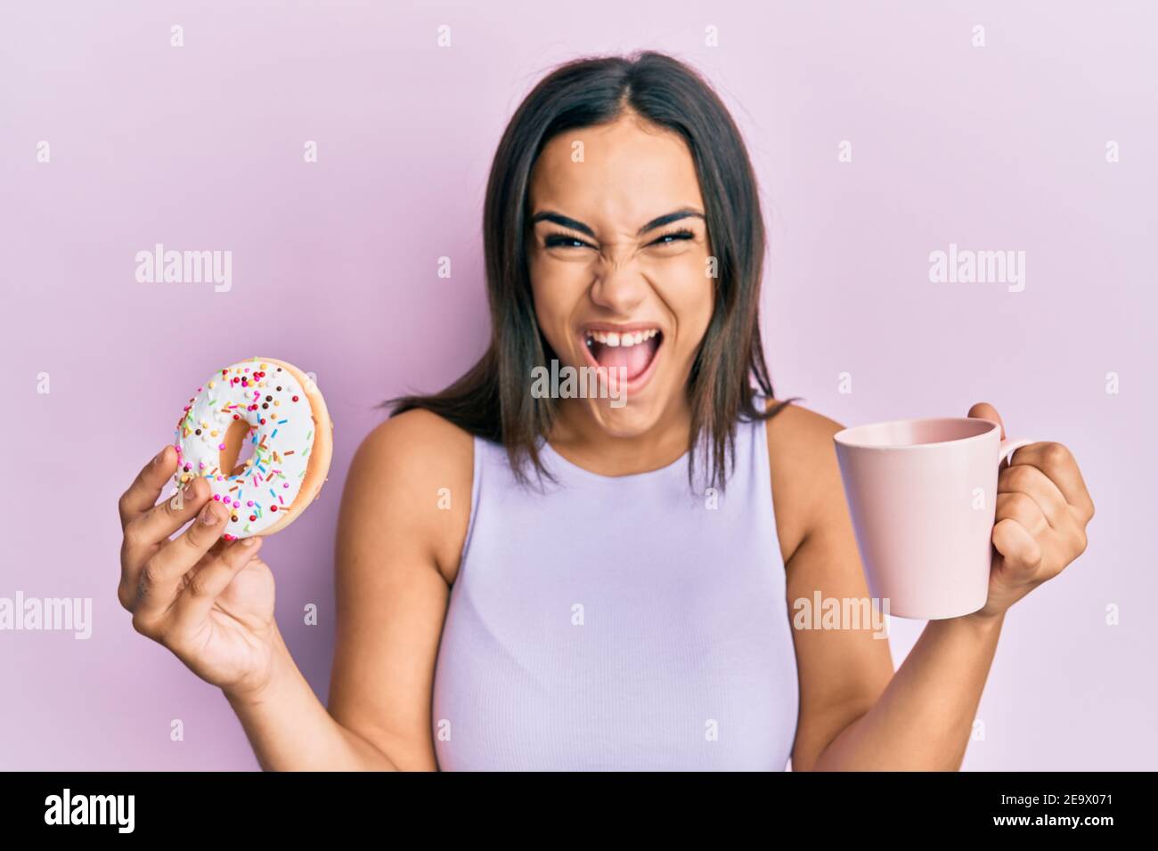 Young brunette woman eating doughnut and drinking coffee celebrating ...