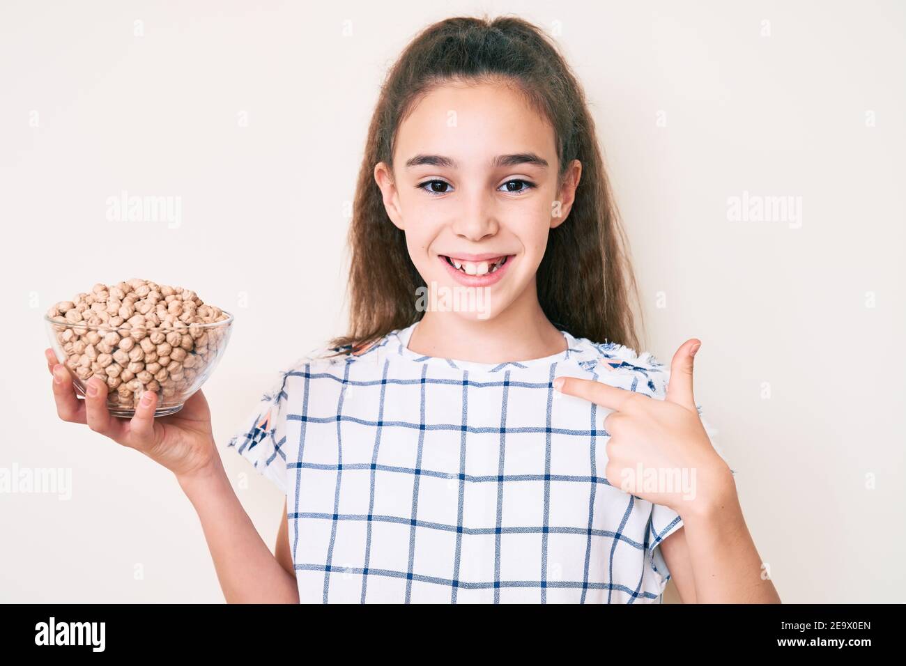 Cute hispanic child girl holding chickpeas bowl pointing finger to one ...