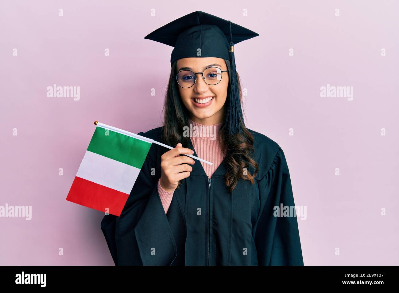 Young hispanic woman wearing graduation uniform holding italy flag ...