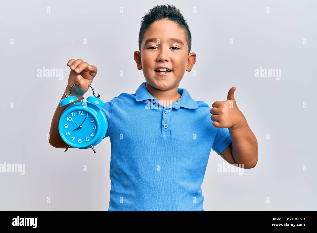 Little boy hispanic kid holding alarm clock smiling happy and positive ...
