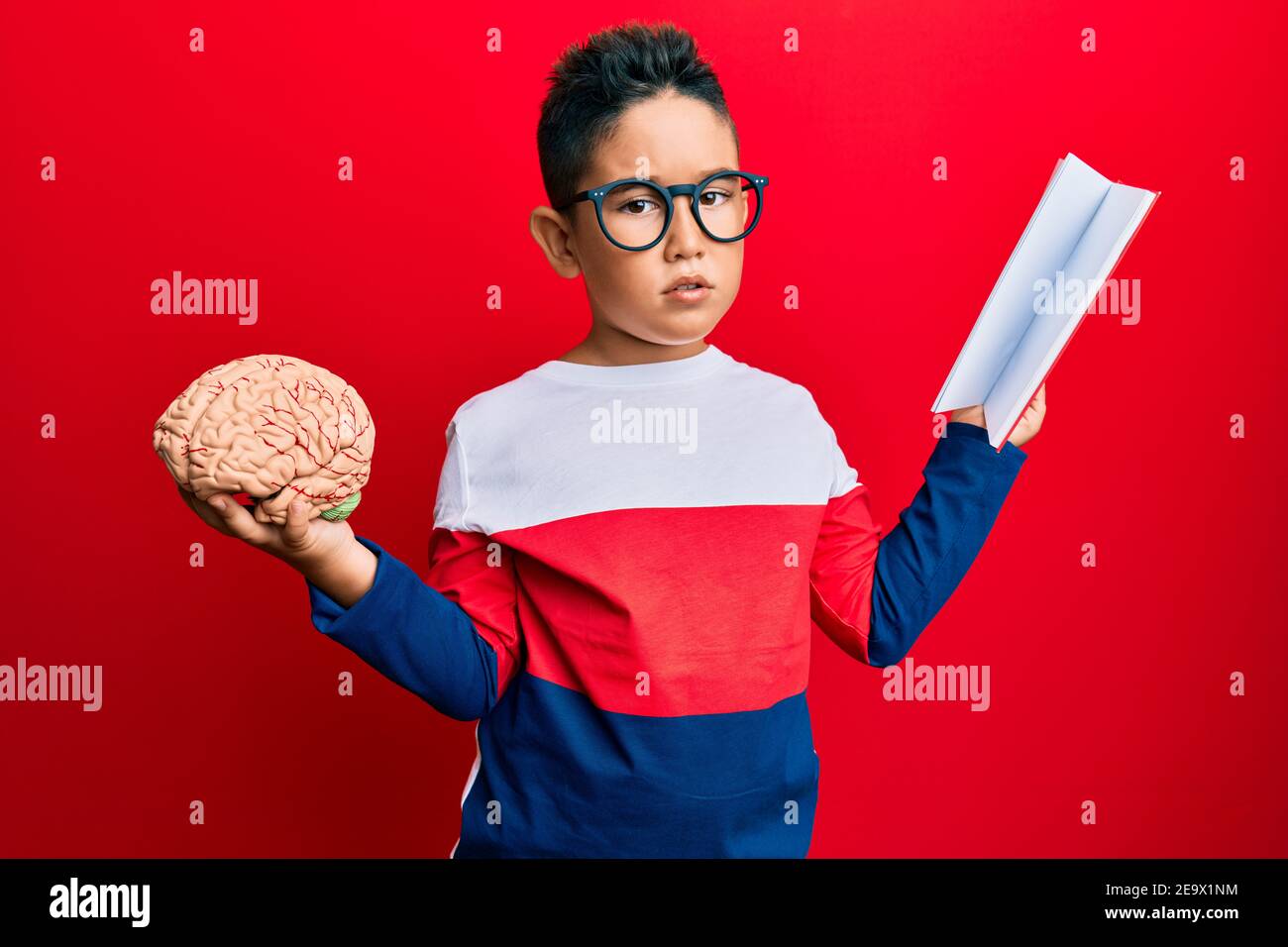 Little boy hispanic kid holding brain studying for school clueless and ...