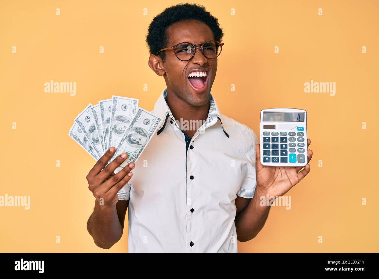 African handsome man holding dollars calculating savings angry and mad ...