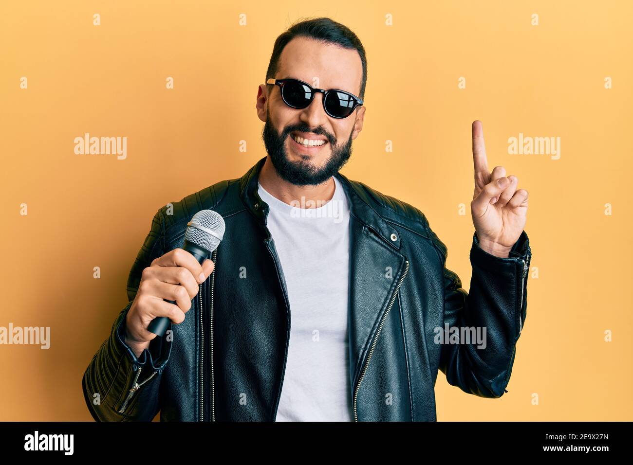 Young man with beard singing song using microphone smiling with an idea ...