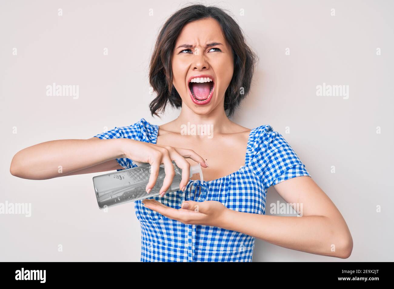 Young beautiful woman using hand sanitizer gel angry and mad screaming ...