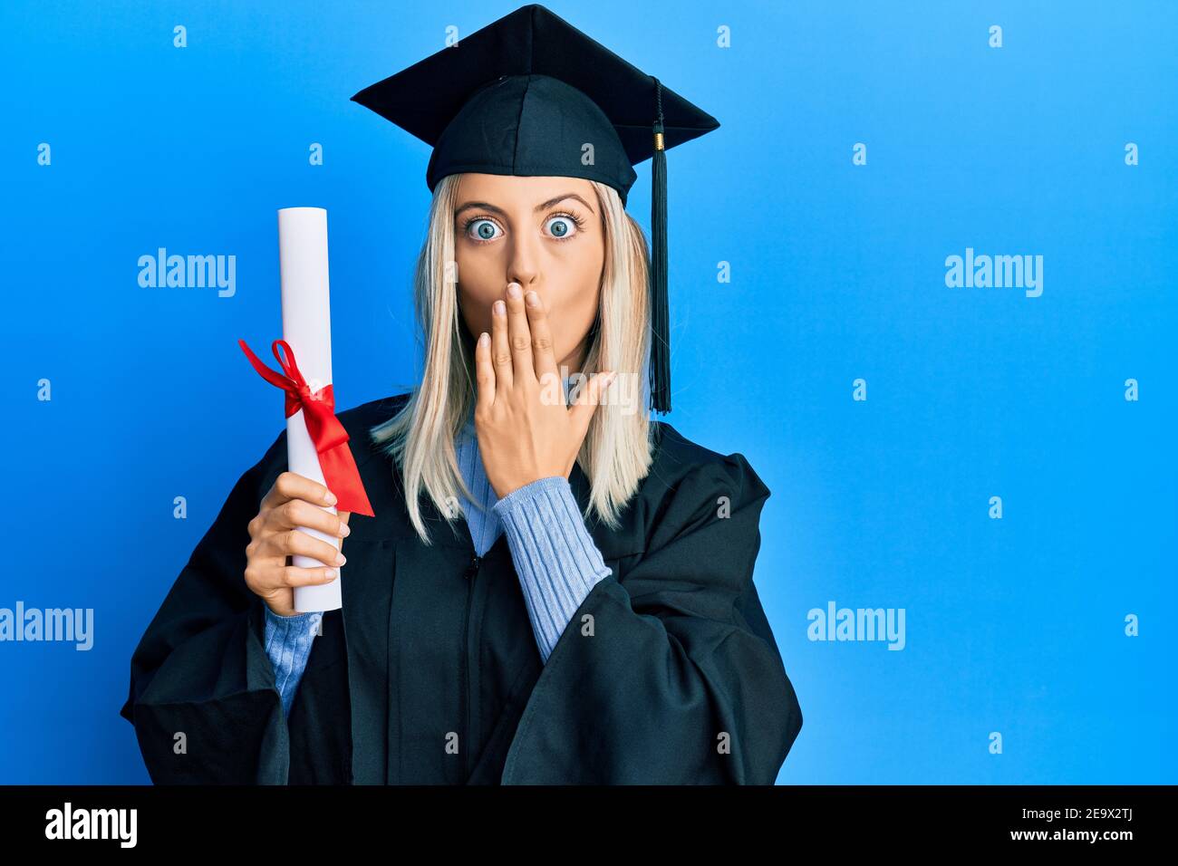 Beautiful blonde woman wearing graduation cap and ceremony robe holding ...