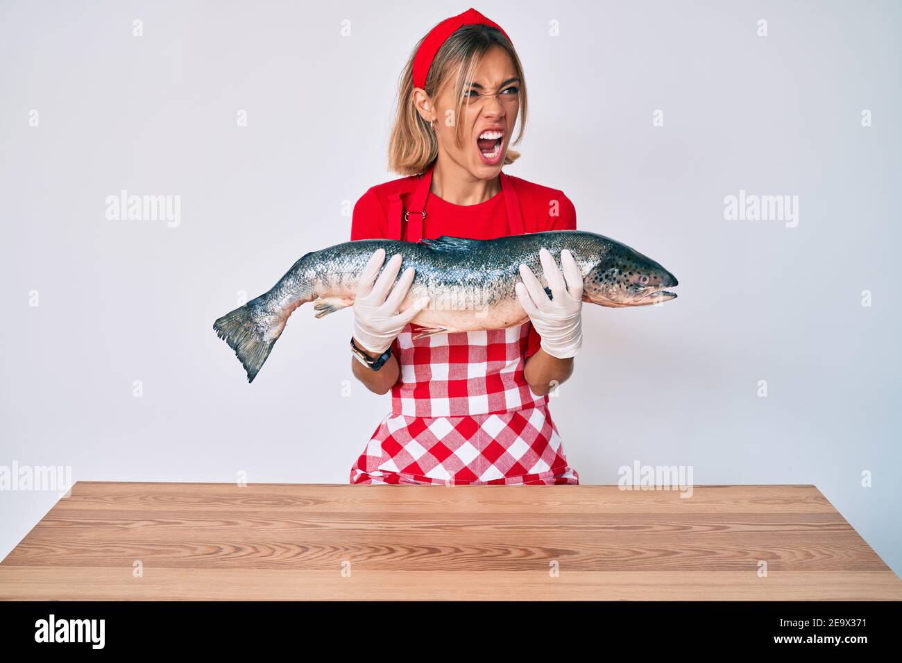 Beautiful caucasian woman fishmonger selling fresh raw salmon angry and ...