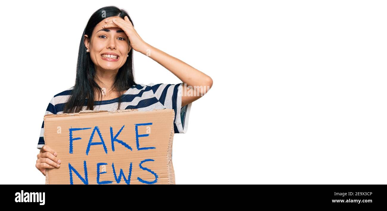Beautiful young woman holding fake news banner stressed and frustrated ...