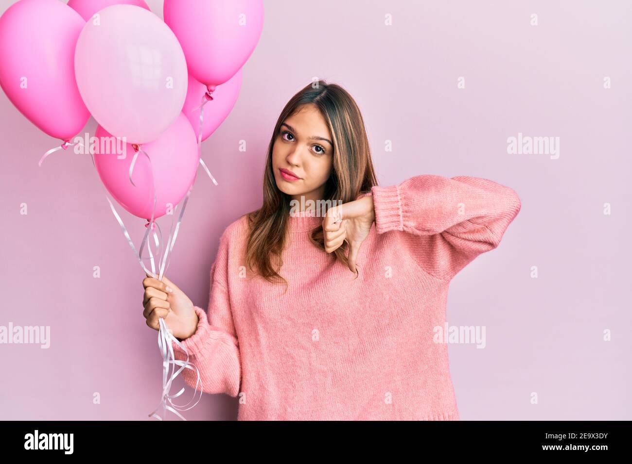 Young brunette woman holding pink balloons with angry face, negative ...