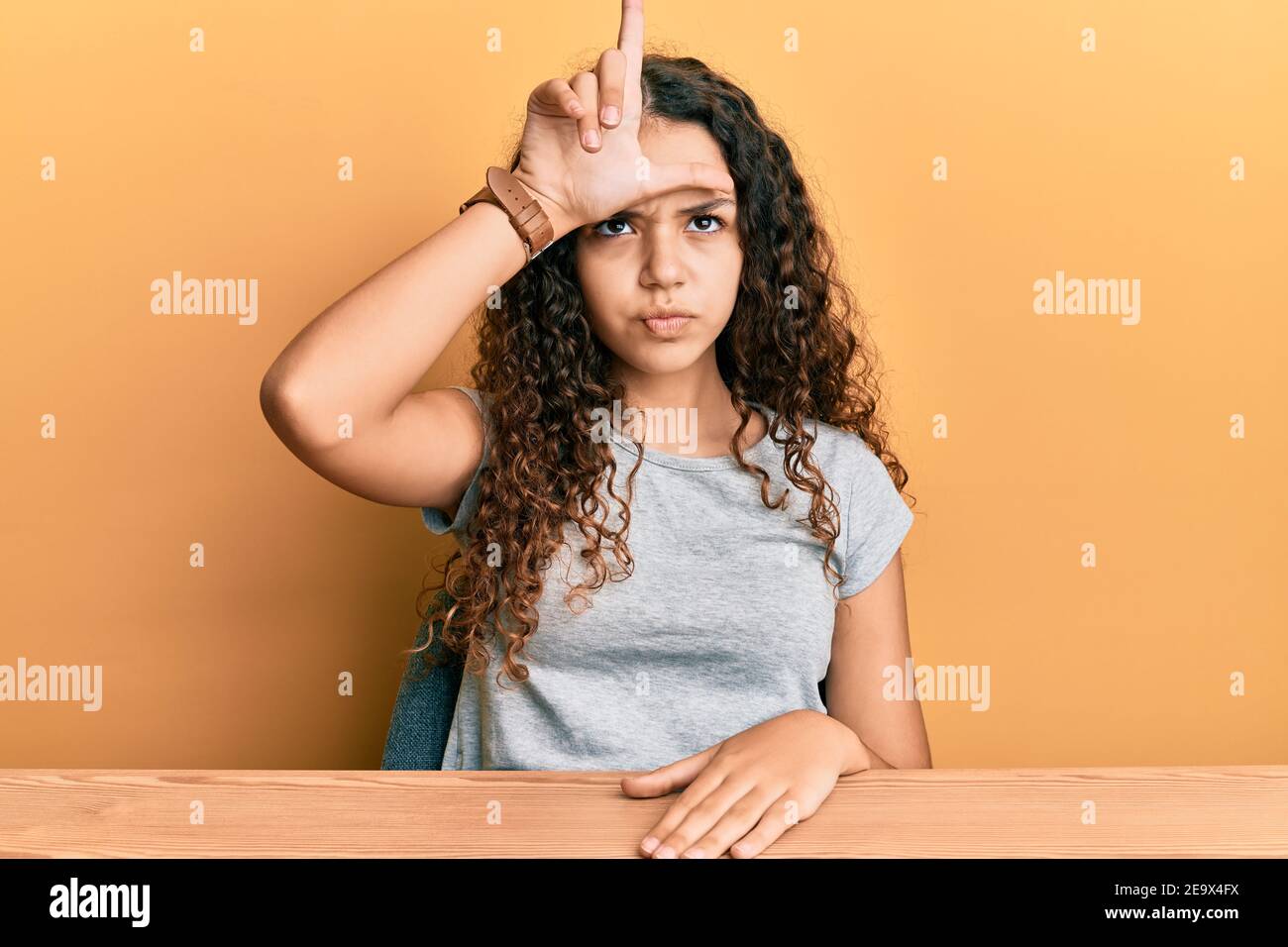 Teenager hispanic girl wearing casual clothes sitting on the table ...