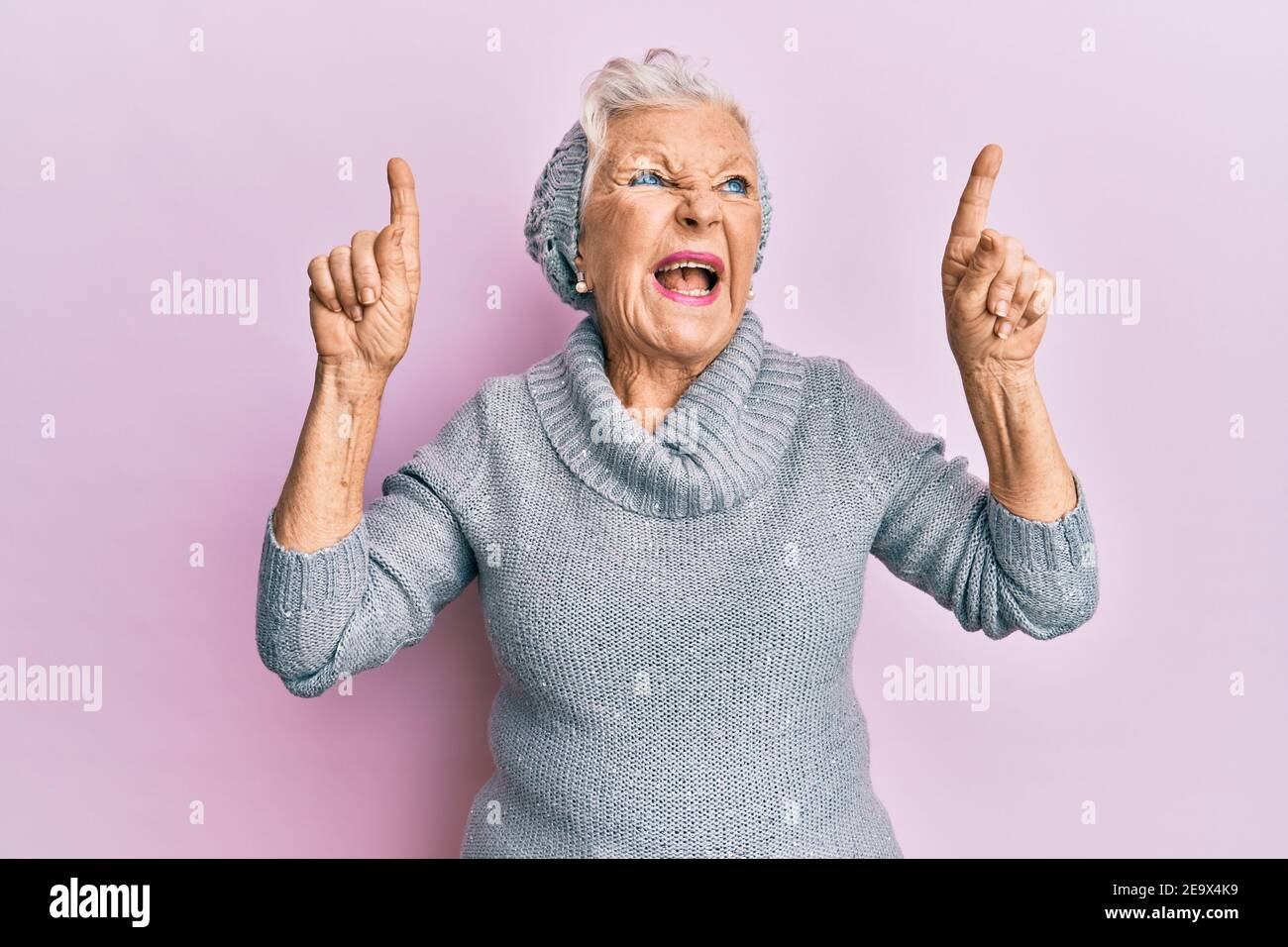 Senior grey-haired woman pointing up with fingers angry and mad ...